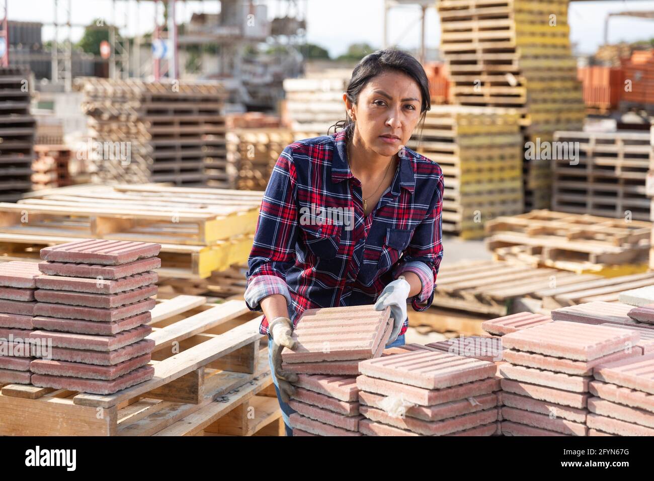 Female worker in gloves sorting red paving slabs in warehouse of ...