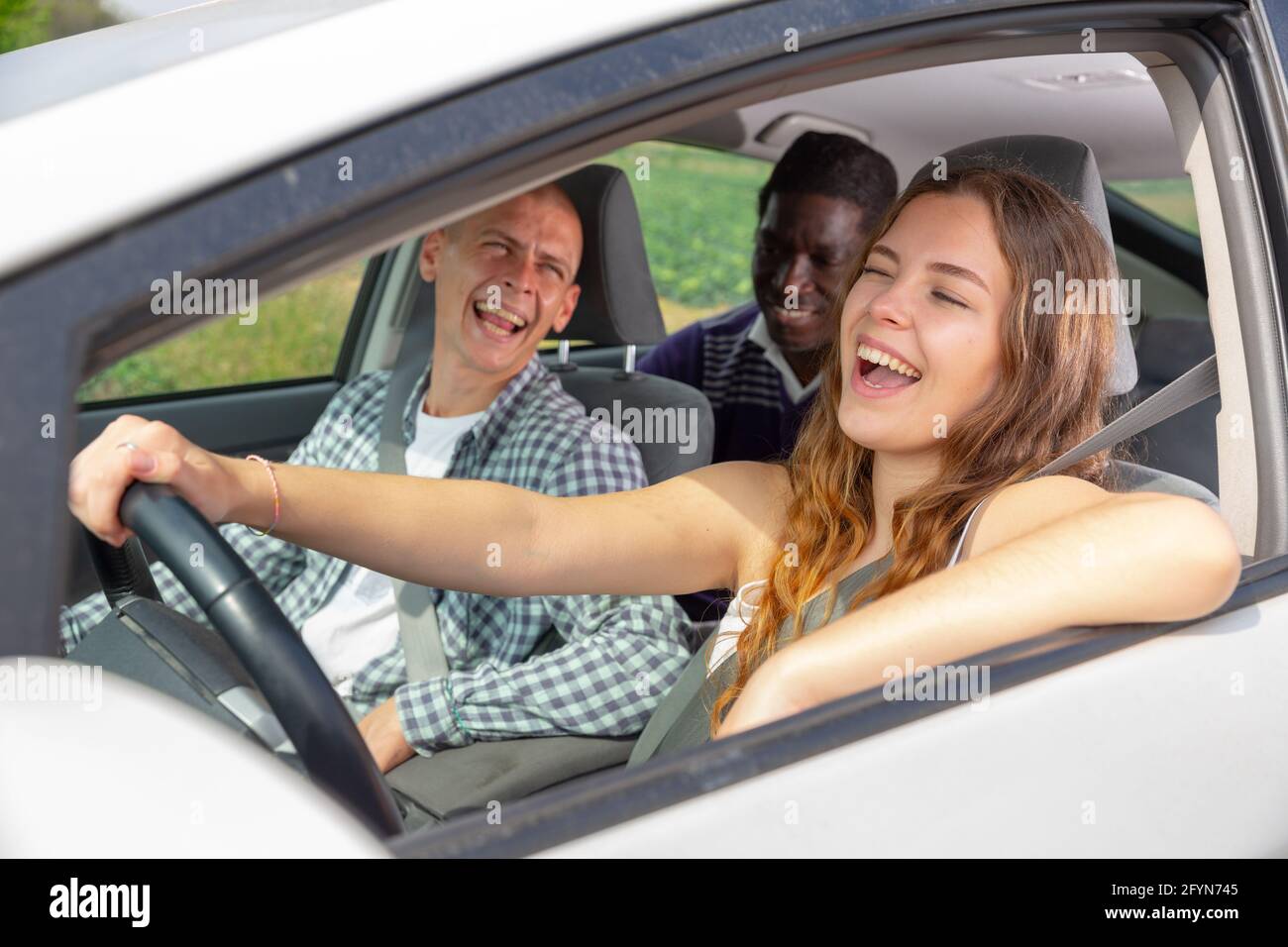 Cheerful young woman driving car with laughing male friends in ...