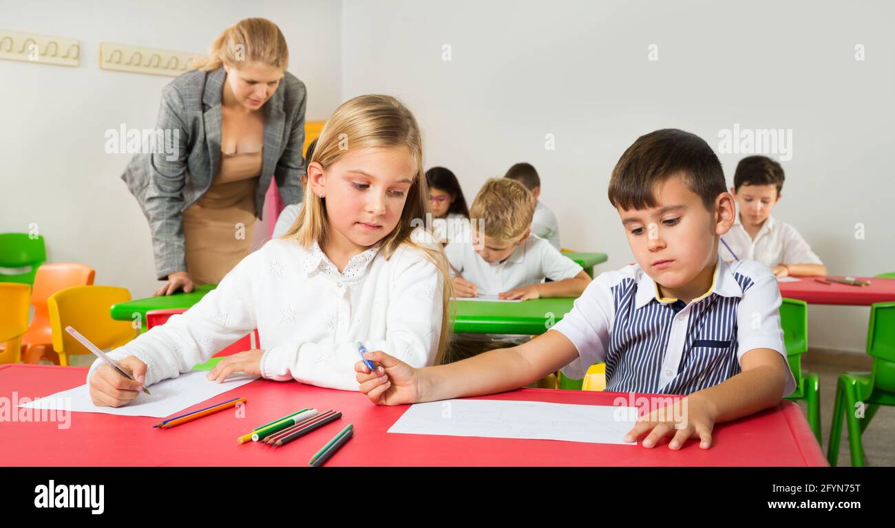 Group of school kids with pens and notebooks studying at a classroom ...