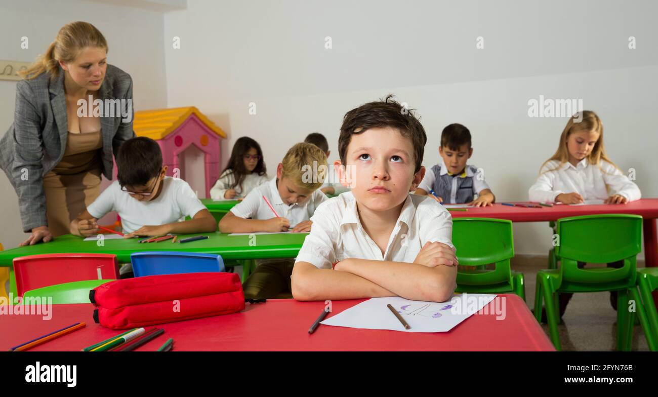Portrait of upset boy in schoolroom on background with pupils studying ...
