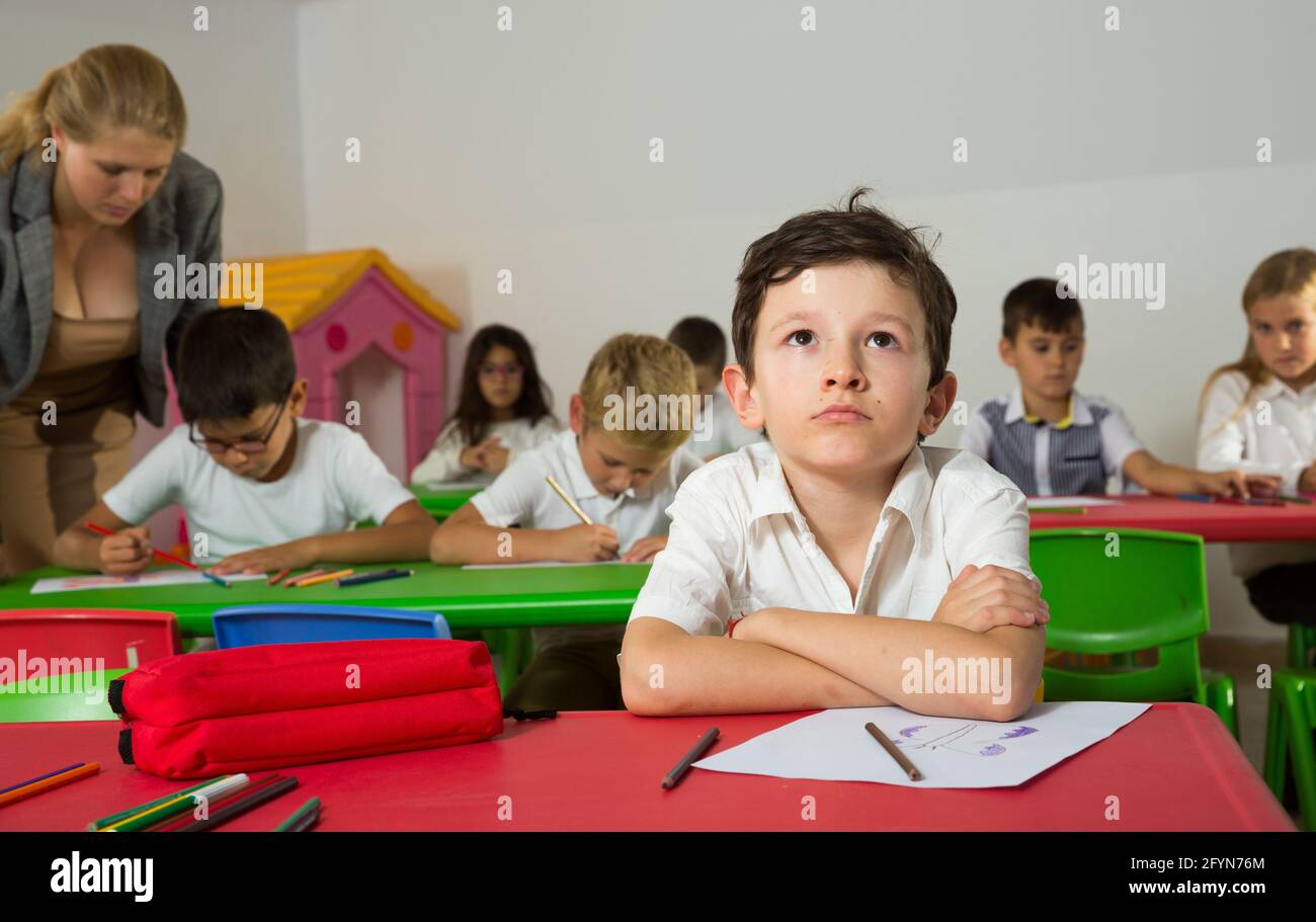 Portrait of upset boy in schoolroom on background with pupils studying ...