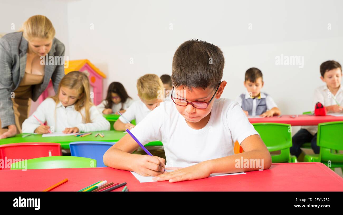 Portrait of boy student of primary school doing his task at desk in ...