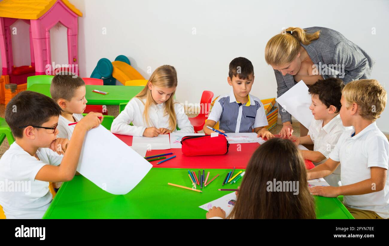 Happy smiling female teacher helping schoolkids drawing with color ...