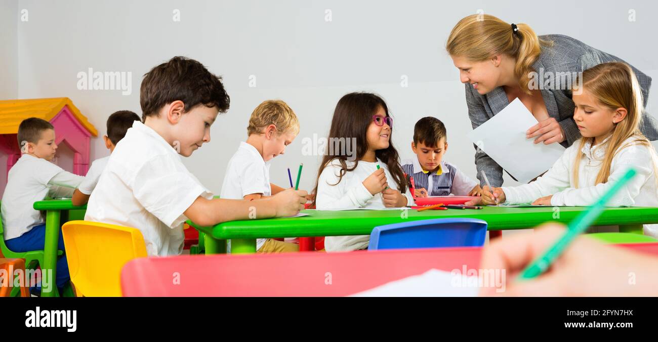 Glad smiling female teacher helping schoolkids drawing with color ...