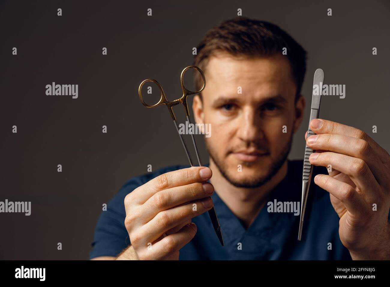 Handsome doctor with surgical scissors and needle holder. Confident man ...