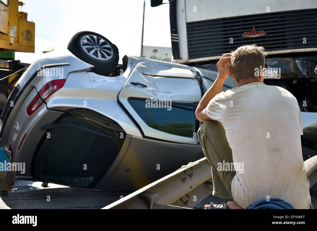 A man sits near a wrecked Renault Tuareg car after a collision with MAZ ...