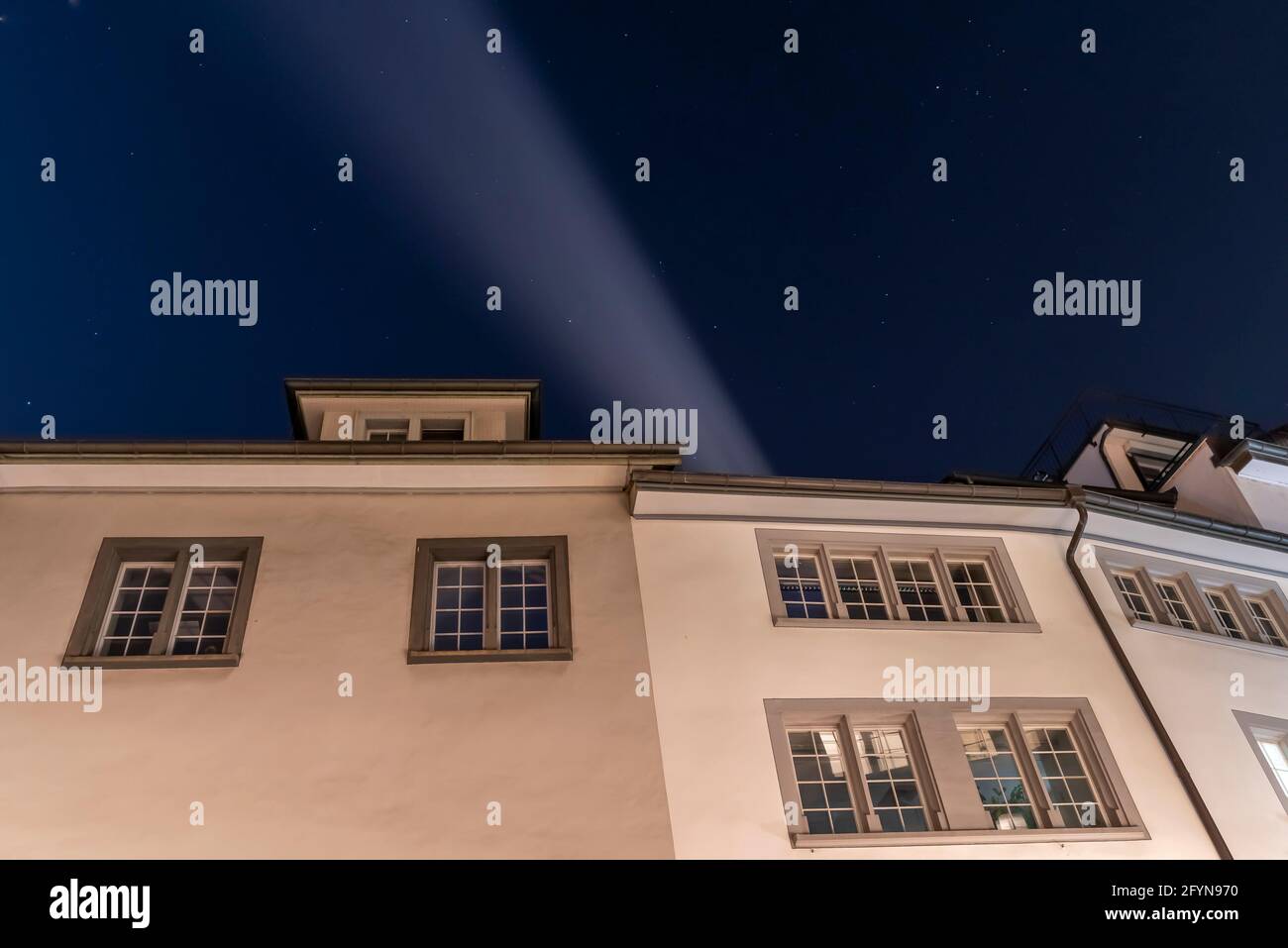 A beam of light from the attic window into the night sky above the ...