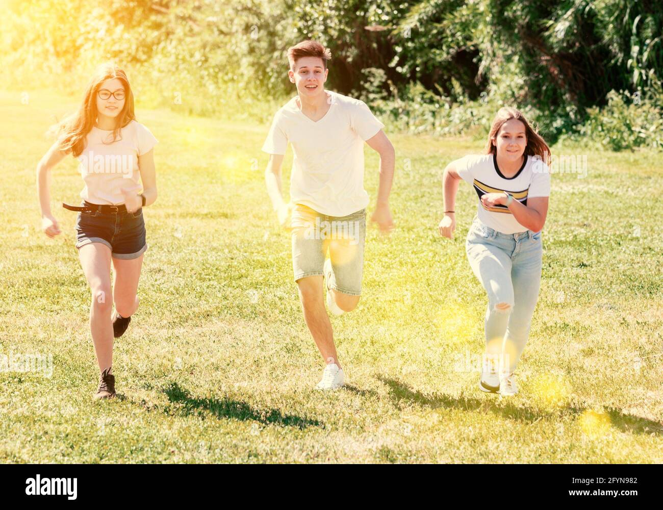 Group of cheerful teenagers running together in summer city park. Happy ...