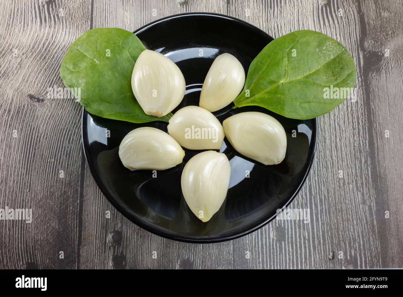 Heads of natural peeled garlic and lettuce leaves on a black plate ...