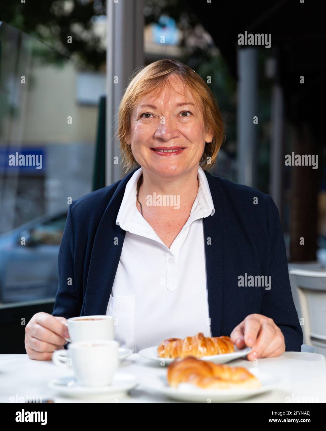 Portrait of smiling elderly woman drinking coffee in modern city cafe ...
