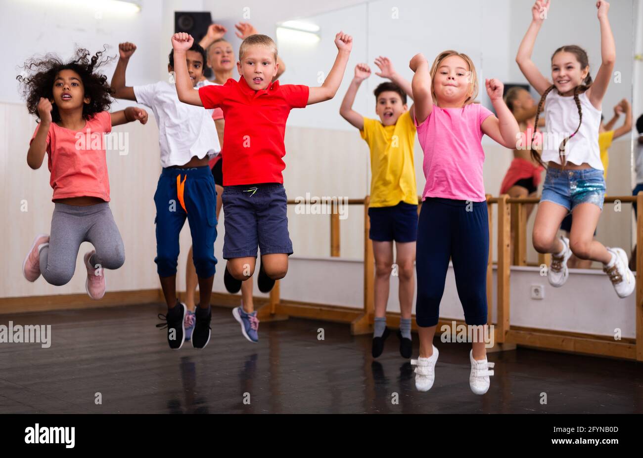Group of cheerful tweens jumping with female trainer during modern ...