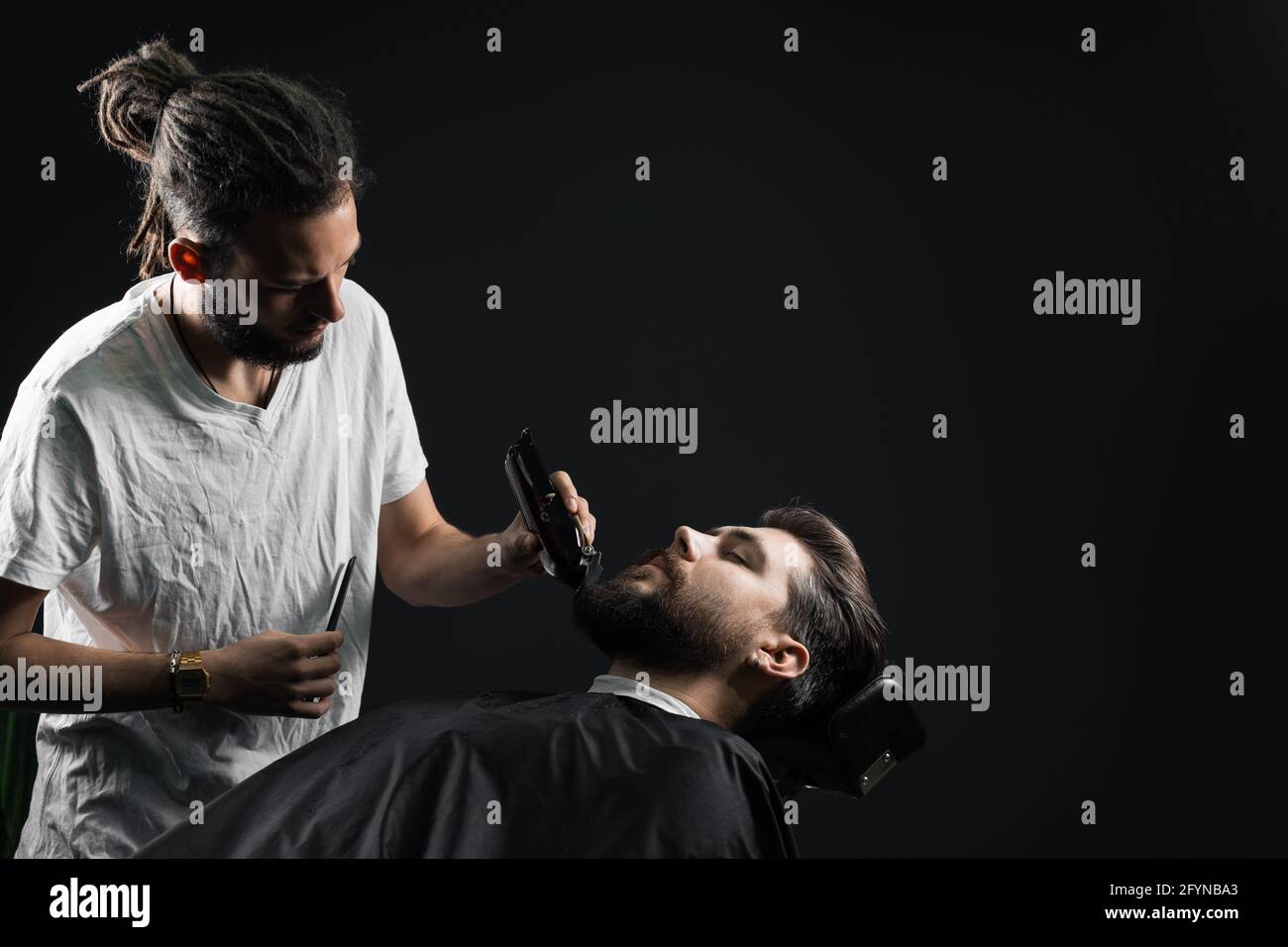 Beard shaving in barbershop. Barber with dreadlocks trim handsome ...