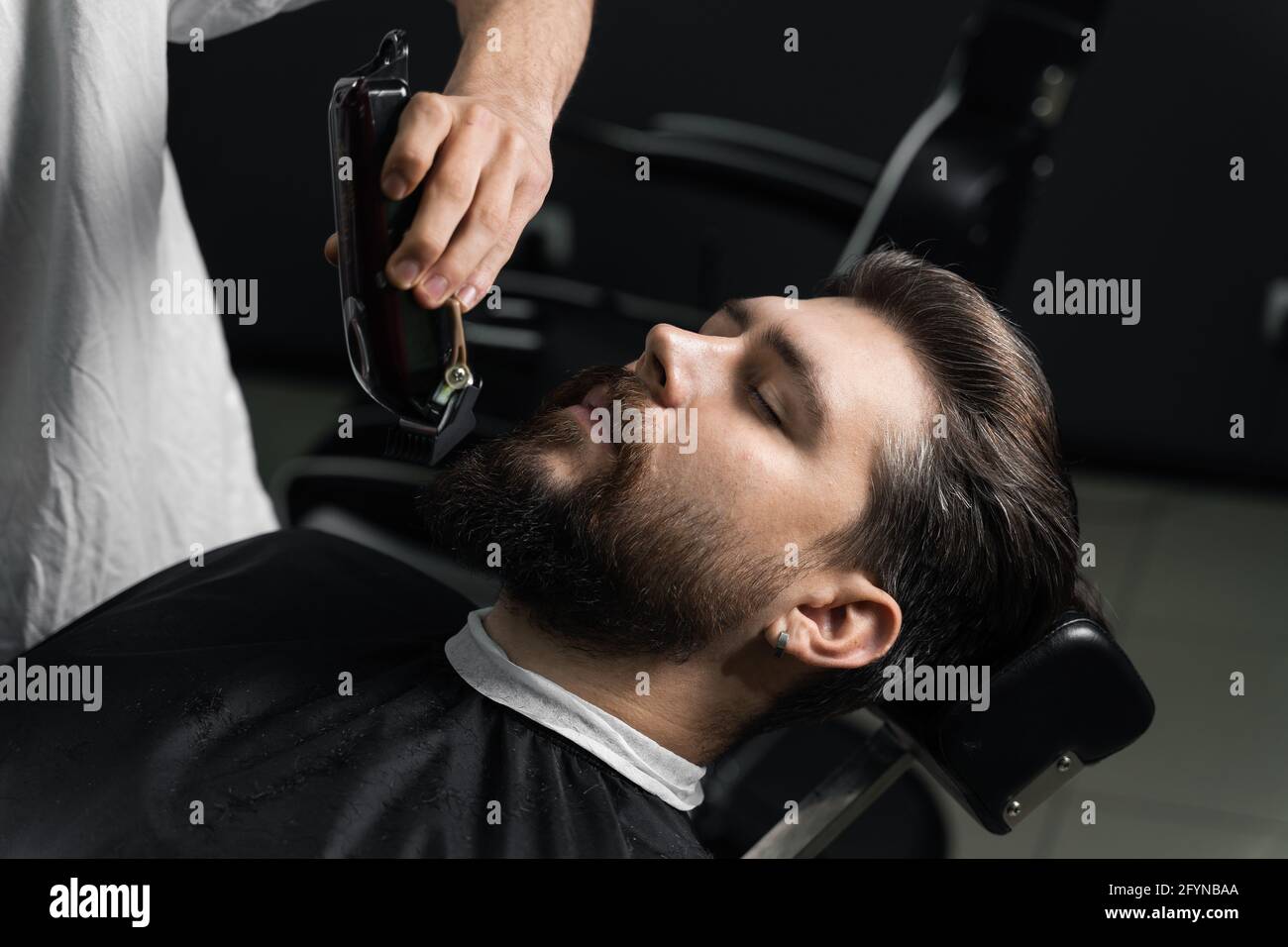 Beard shaving in barbershop. Barber with dreadlocks trim handsome ...