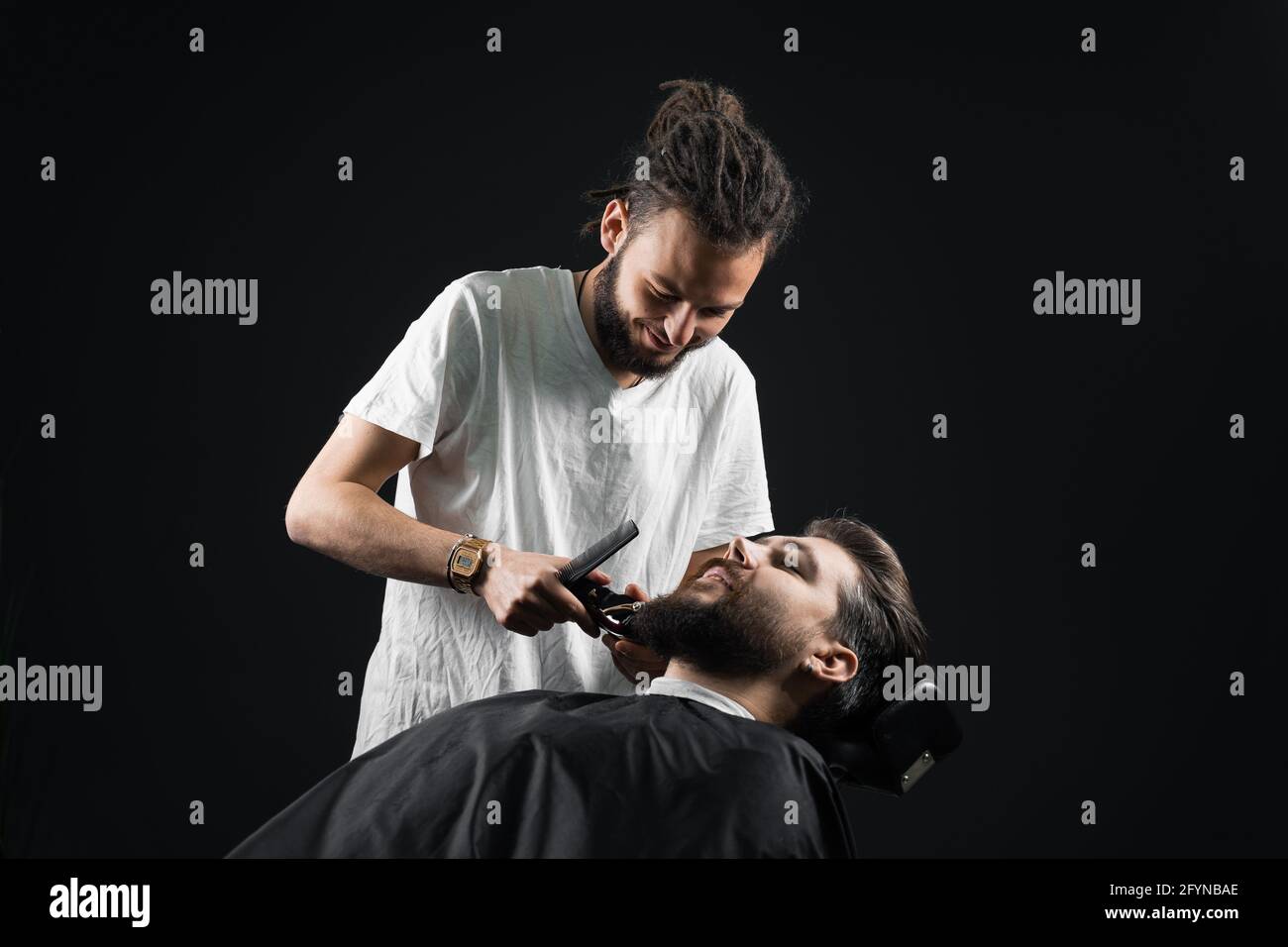 Beard shaving in barbershop. Barber with dreadlocks trim handsome ...