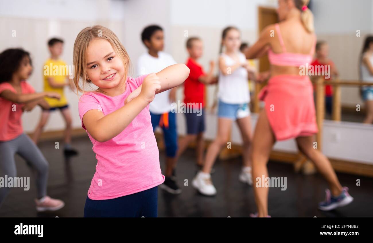 Smiling little girl training movements of vigorous dance with group of ...