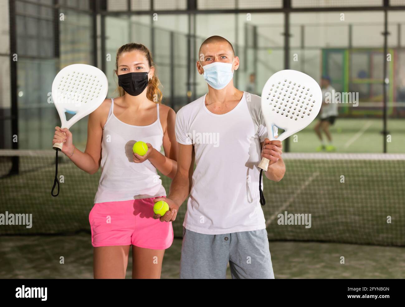 Confident couple of young paddle tennis players wearing protective face ...