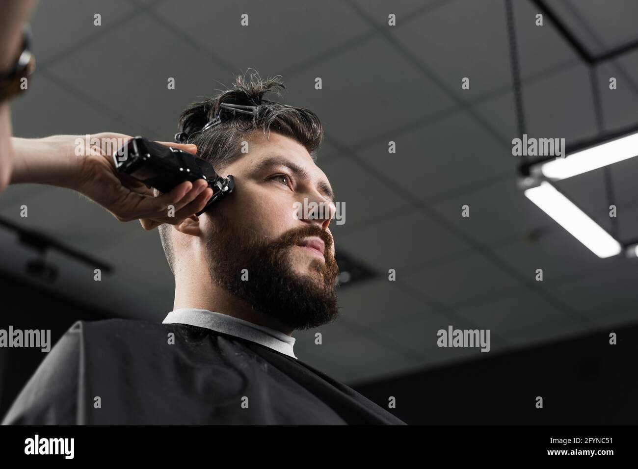 Low fade machine haircut for handsome bearded man in barbershop. Barber ...