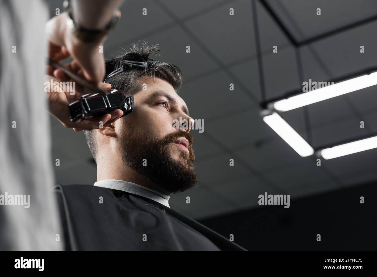 Low fade machine haircut for handsome bearded man in barbershop. Barber ...