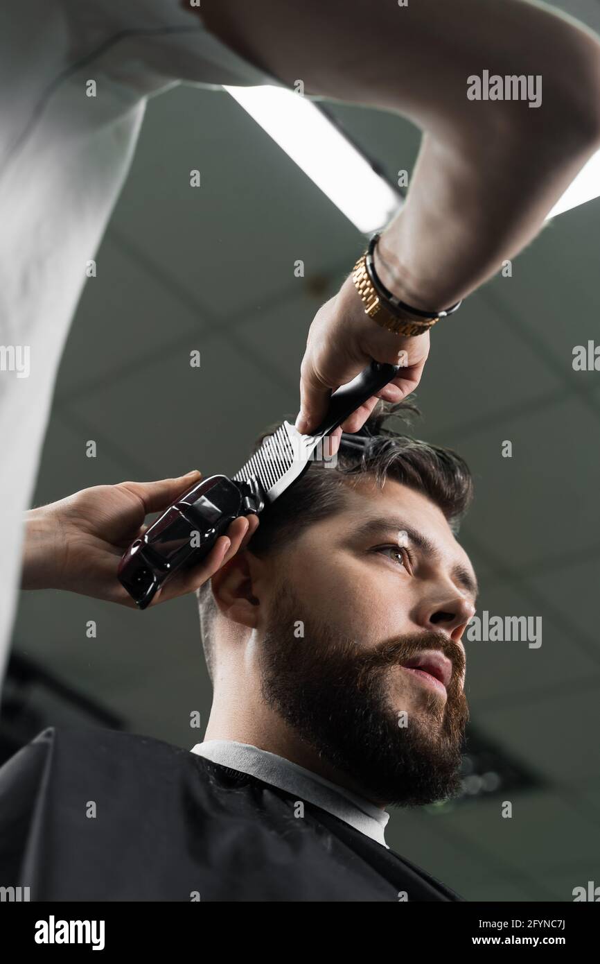 Low fade machine haircut for handsome bearded man in barbershop. Barber ...
