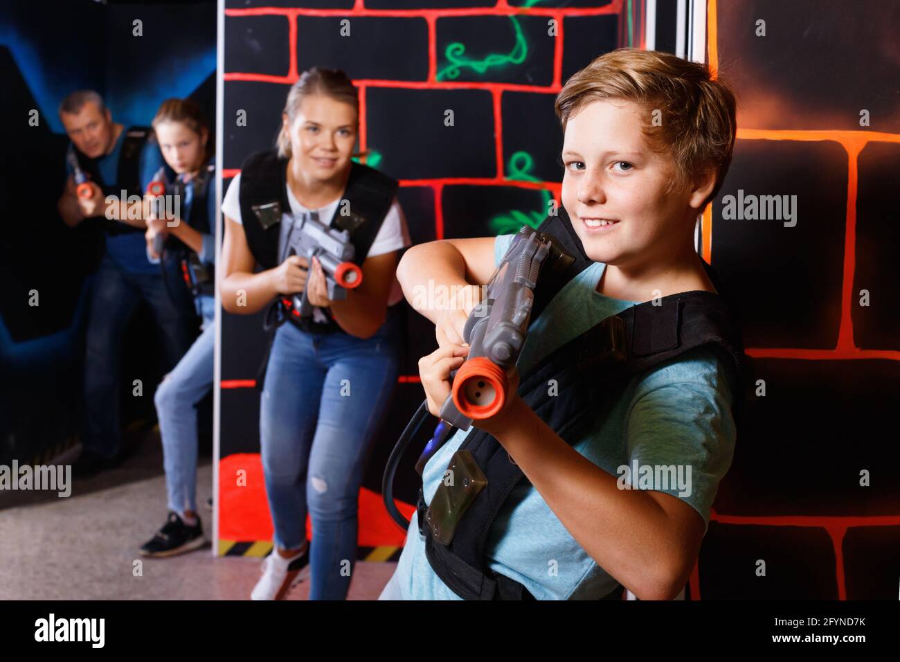 Excited glad cheerful positive boy aiming laser gun at other players ...