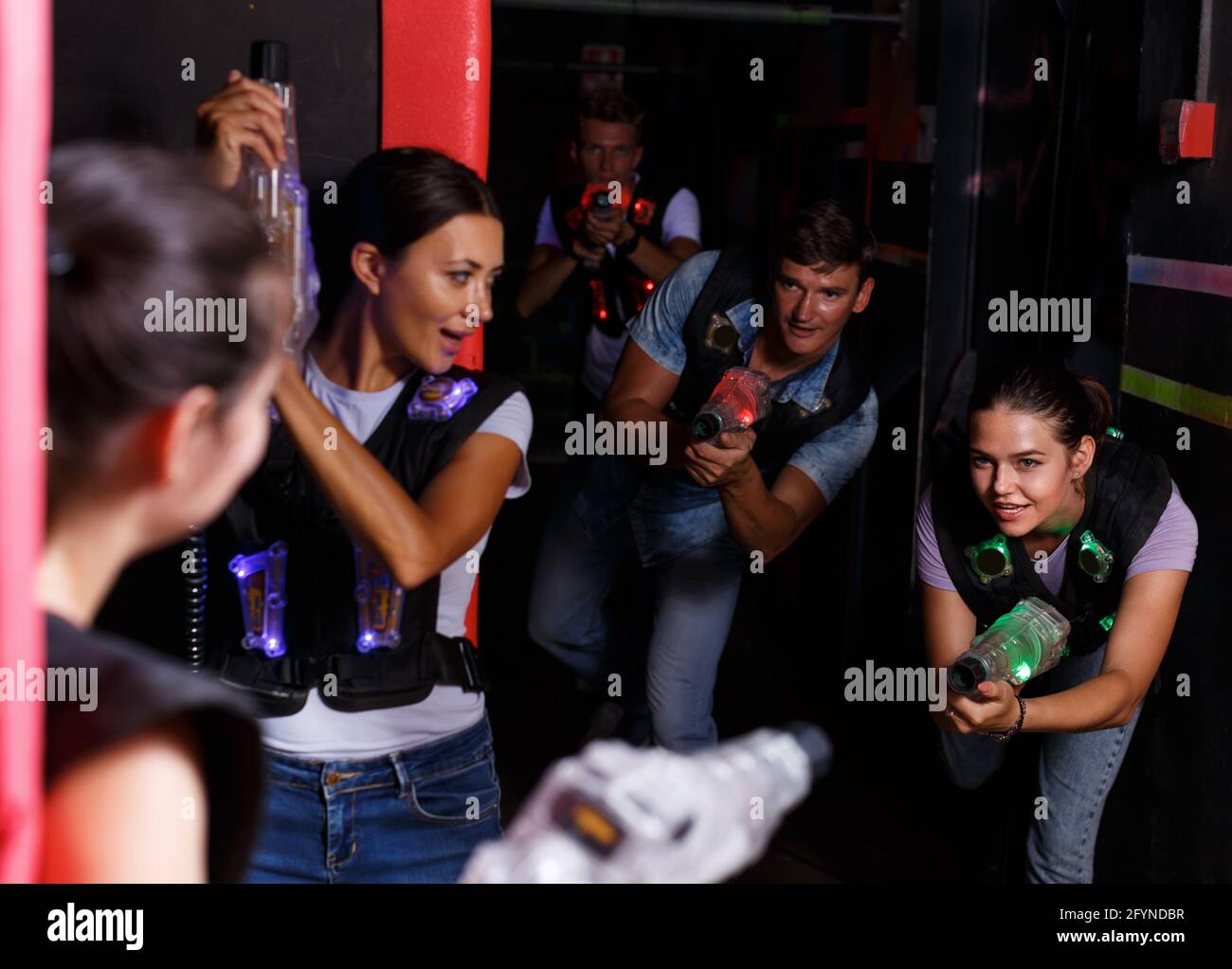 Group of young friends with laser guns playing laser tag game together ...