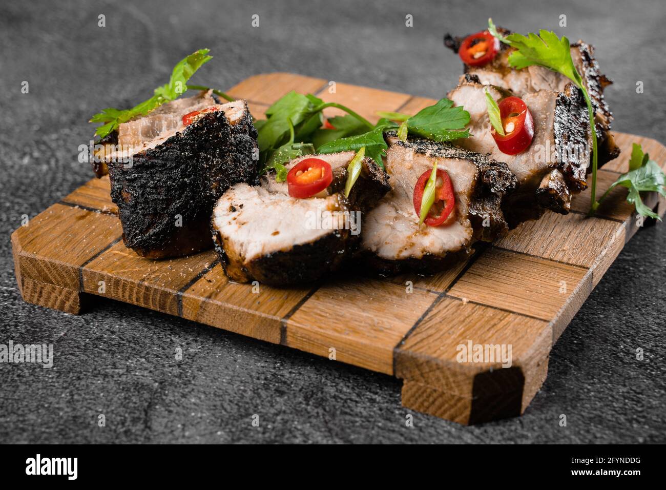 Fried ribs on a wooden plate on a gray background. Barbecue decoration ...