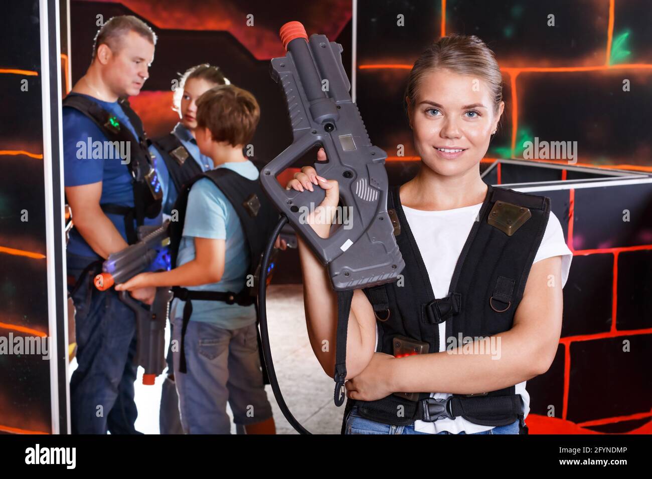 Portrait of happy young woman standing with gun during family laser tag ...