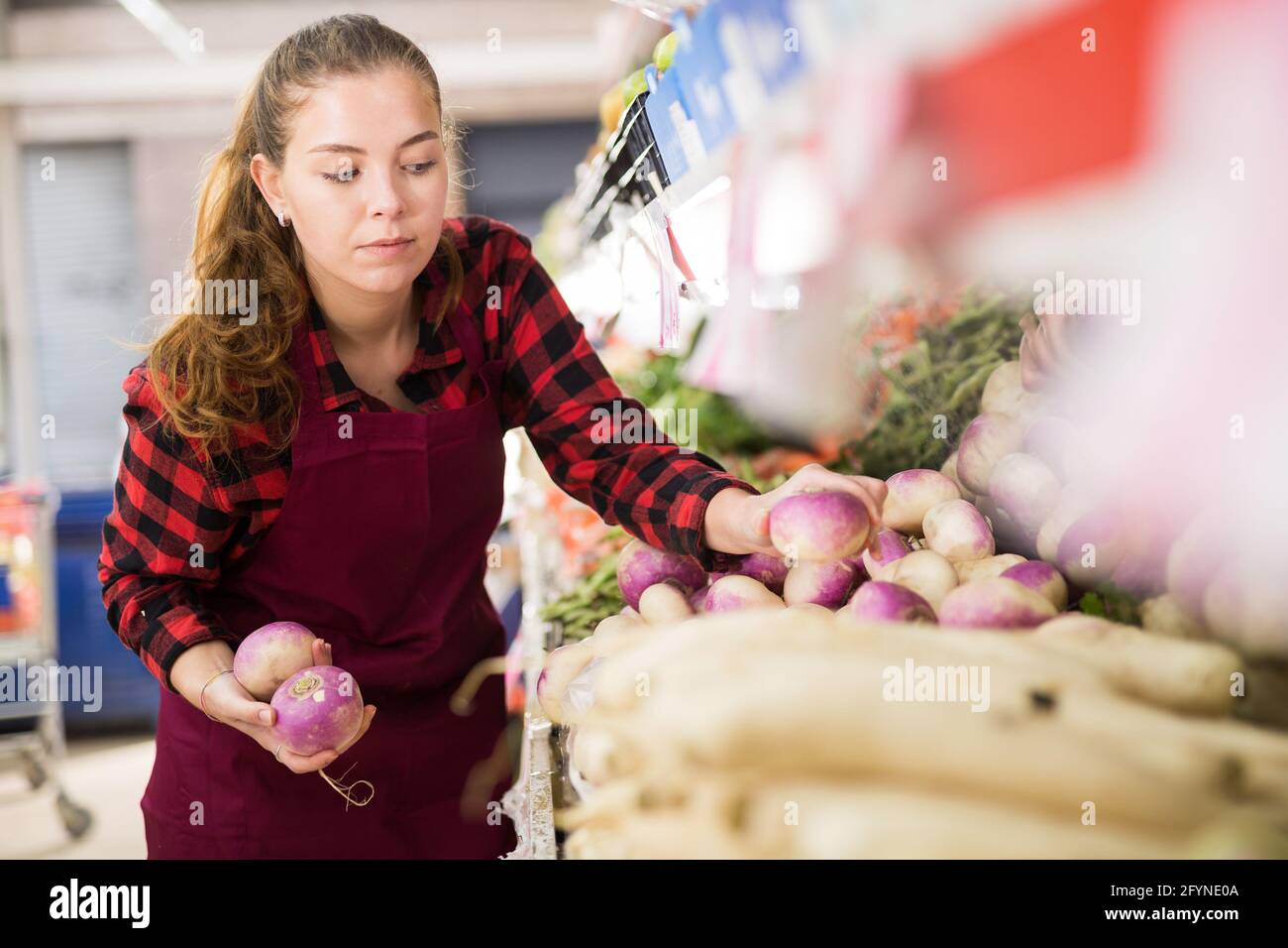 Cheerful female shopping assistant selling purple turnip in grocery ...