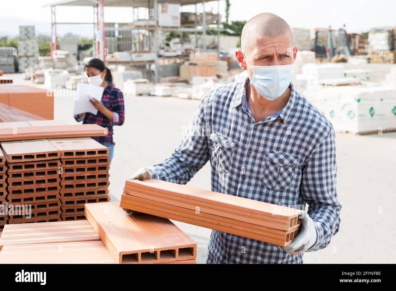 Worker in protecrive mask stacking bricks in warehouse of building ...