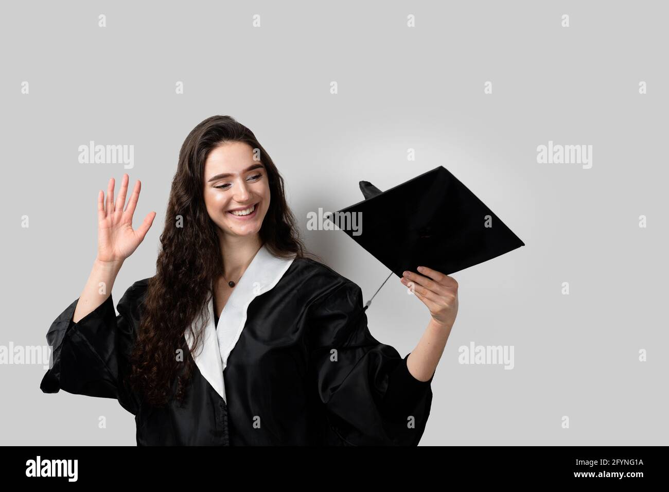 Surprised bachelor girl in graduation robe and cap on white background ...