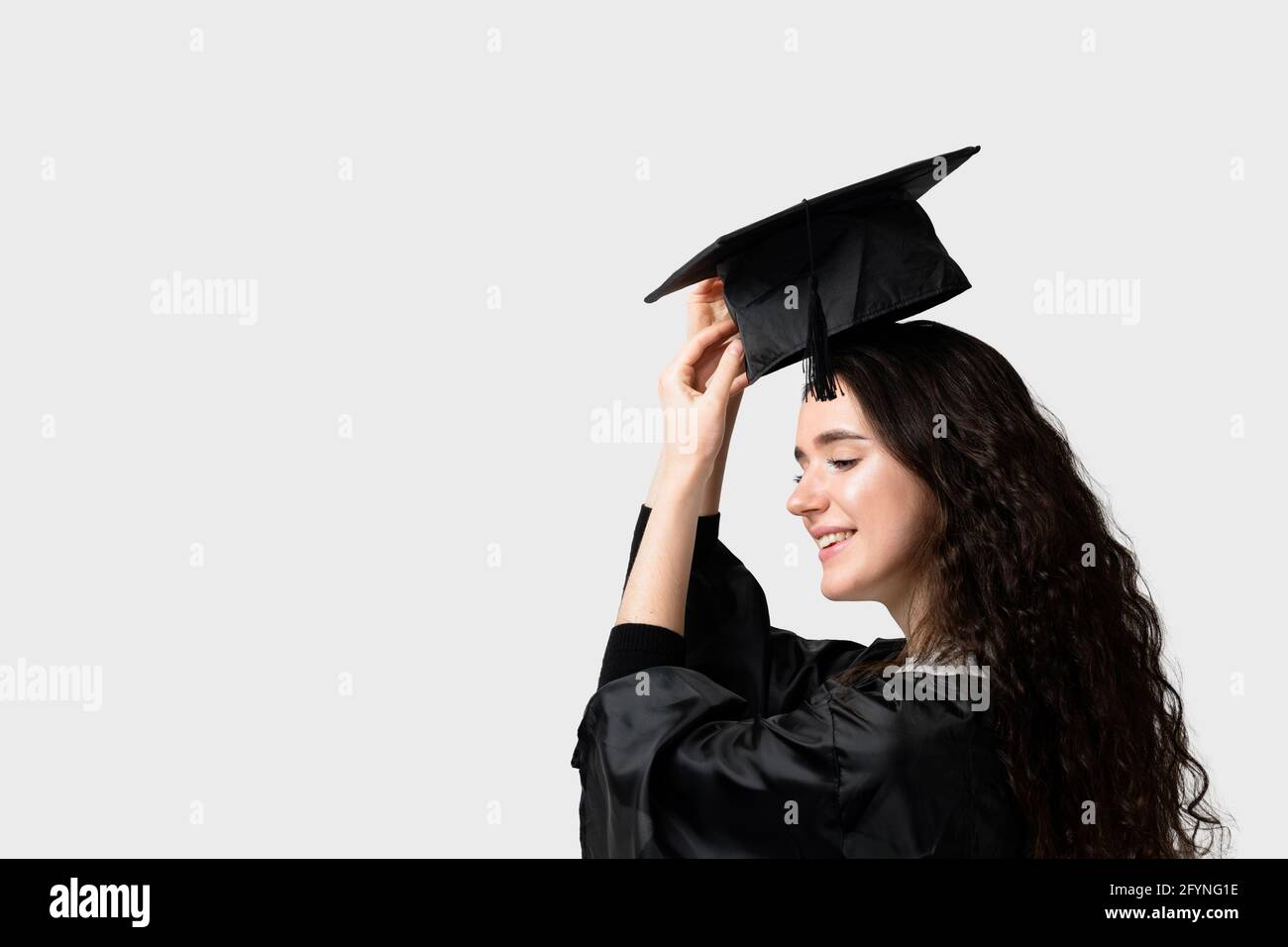 Surprised bachelor girl in graduation robe and cap on white background ...