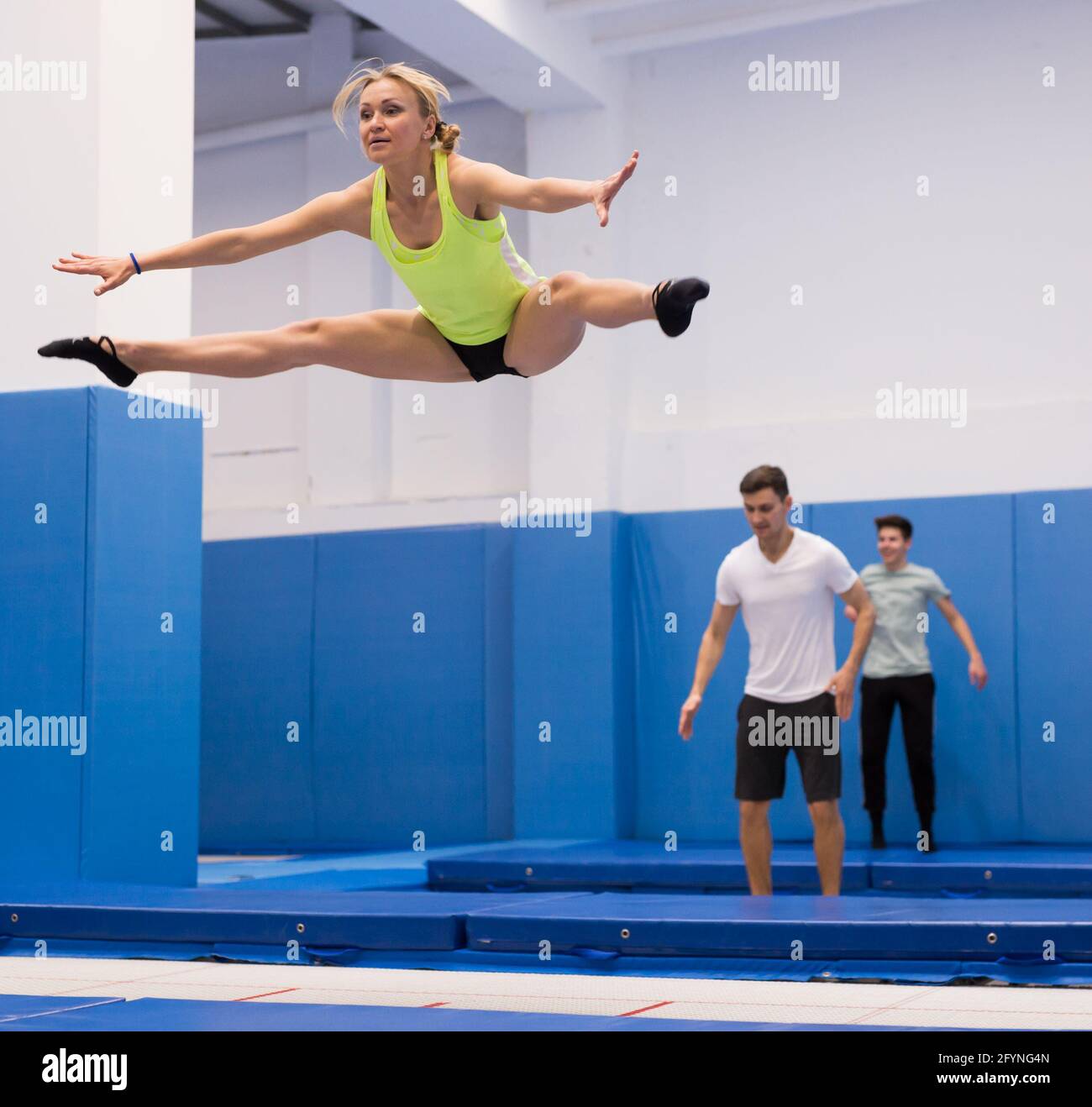 Young athletic woman practicing side split in jump on trampoline in ...