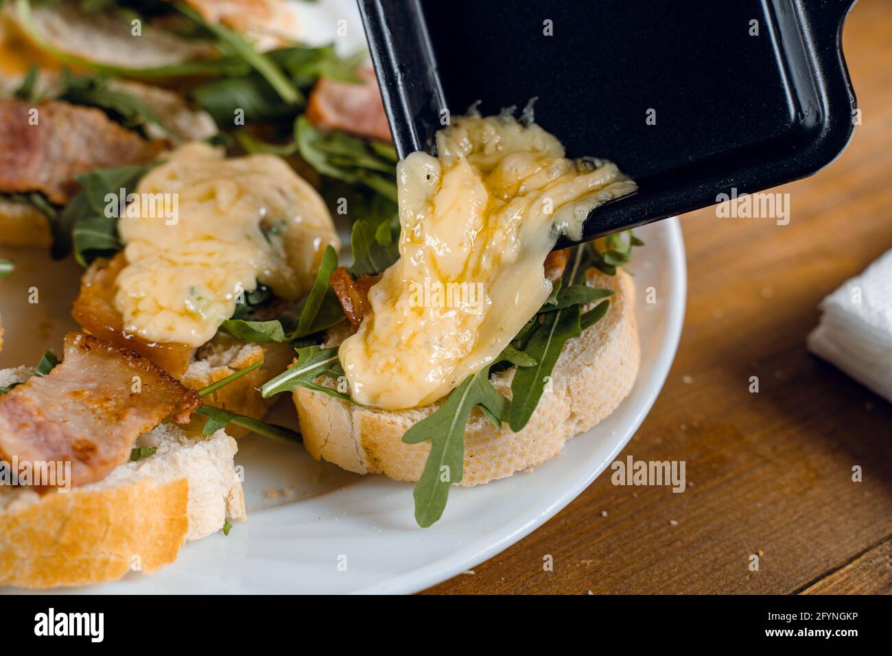 Raclette melted cheese for sandwich with fried bacon and arugula ...
