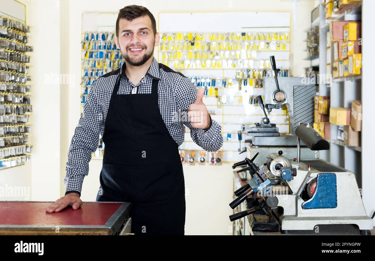 Happy young man worker displaying his tools for making keys in workshop ...