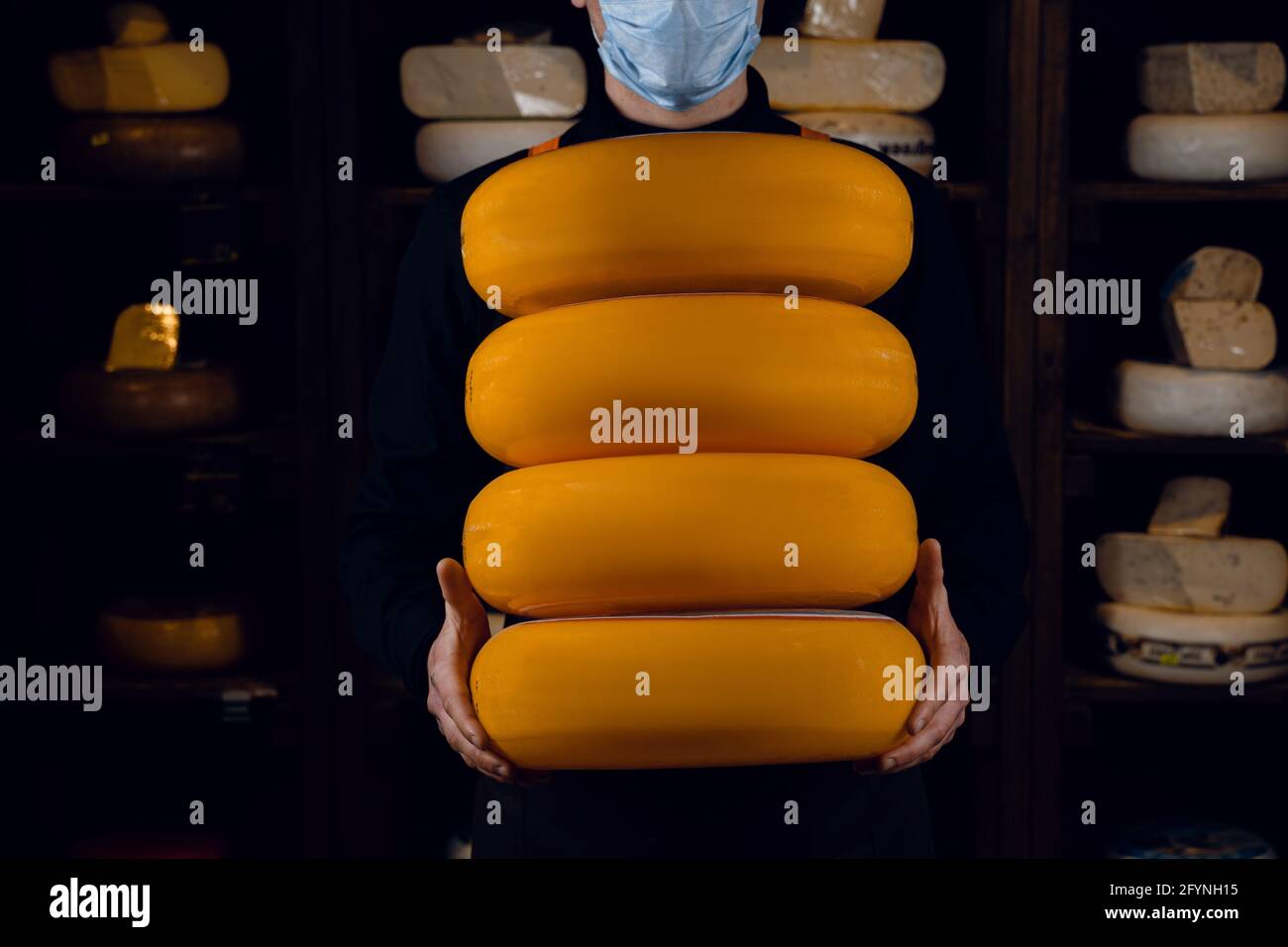 4 Big yellow cheeses wheels in hands. Seller in mask for protection ...