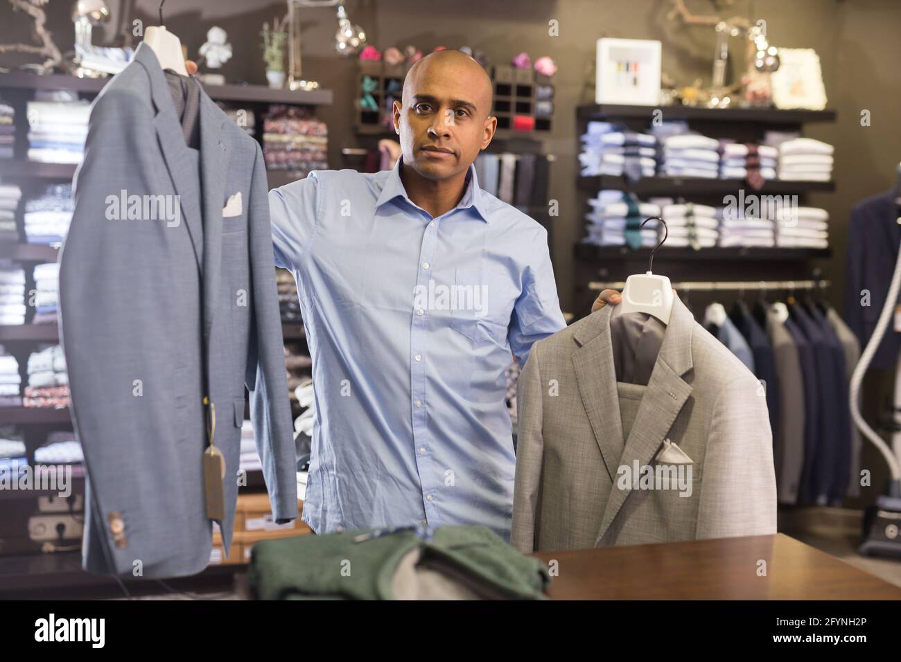 Portrait of young adult male customer choosing suit in clothing store ...