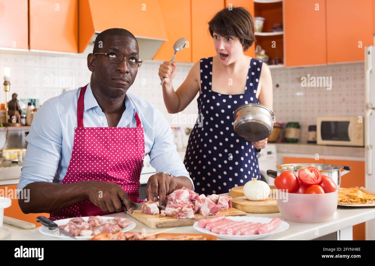 Portrait of upset African man cutting meat for dinner in home kitchen ...