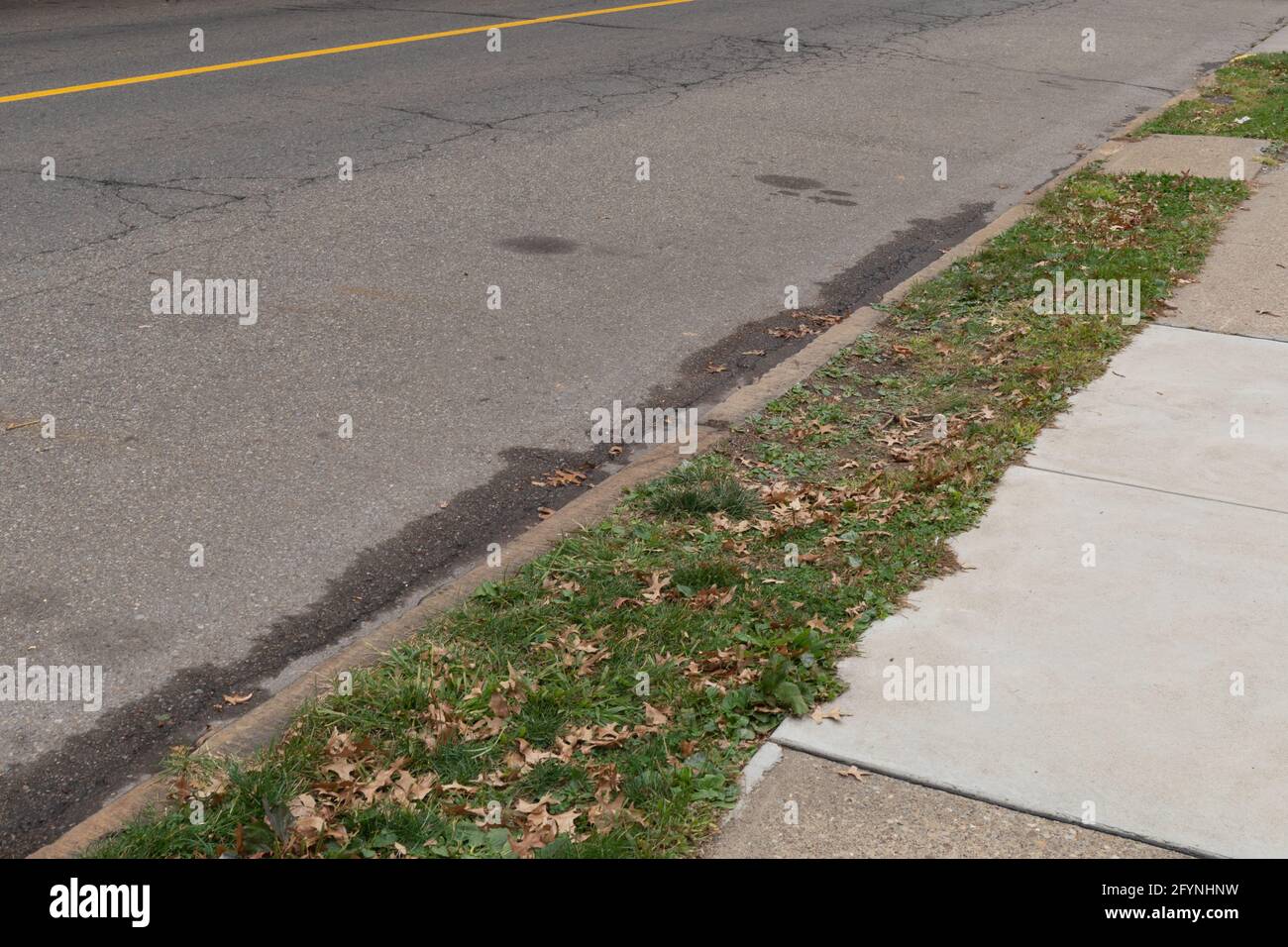 Stained asphalt street with grass strip and concrete sidewalk ...