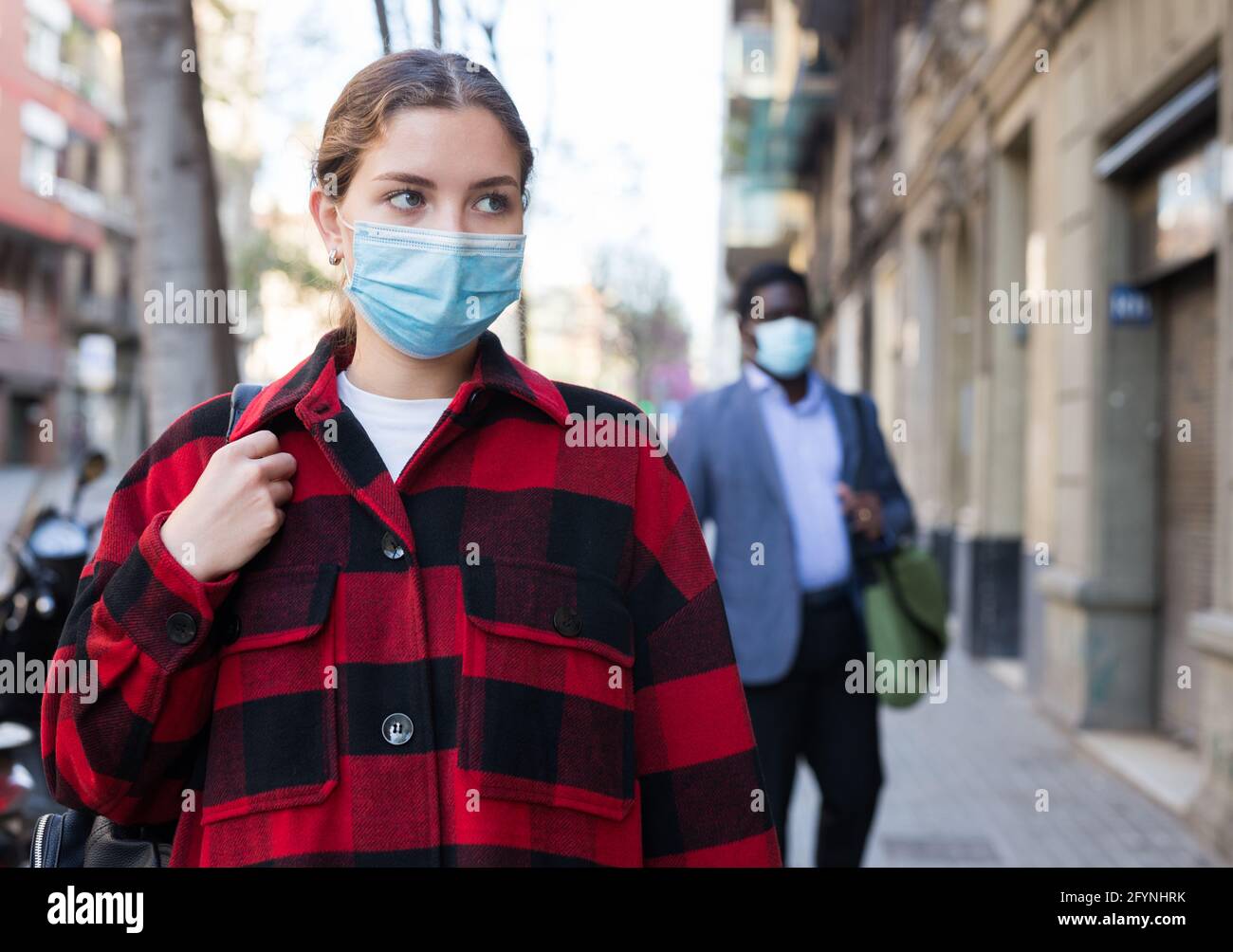 Young woman in disposable face mask walking along city street. Concept ...