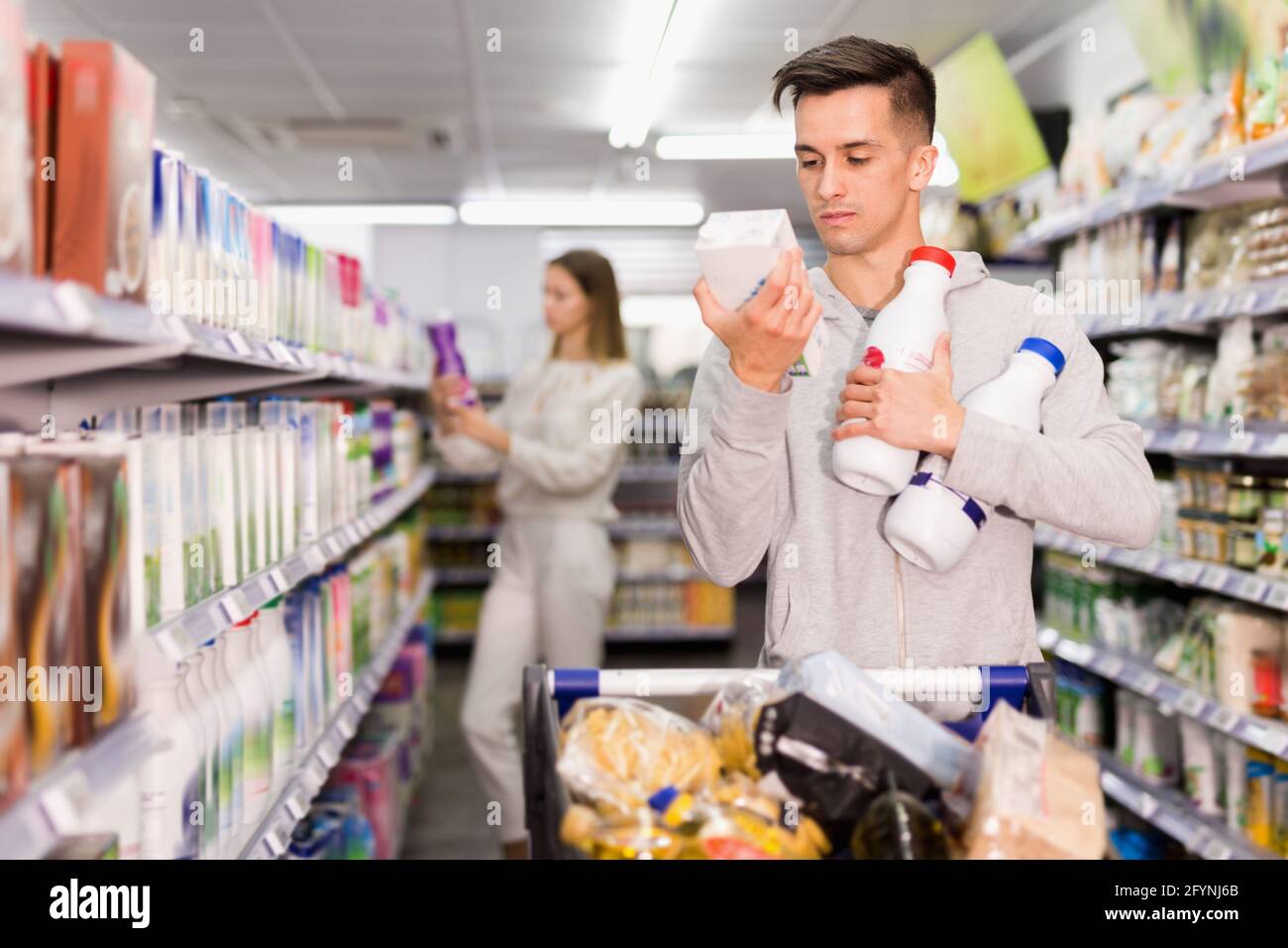 Young glad positive male customer choosing milk and dairy products in ...