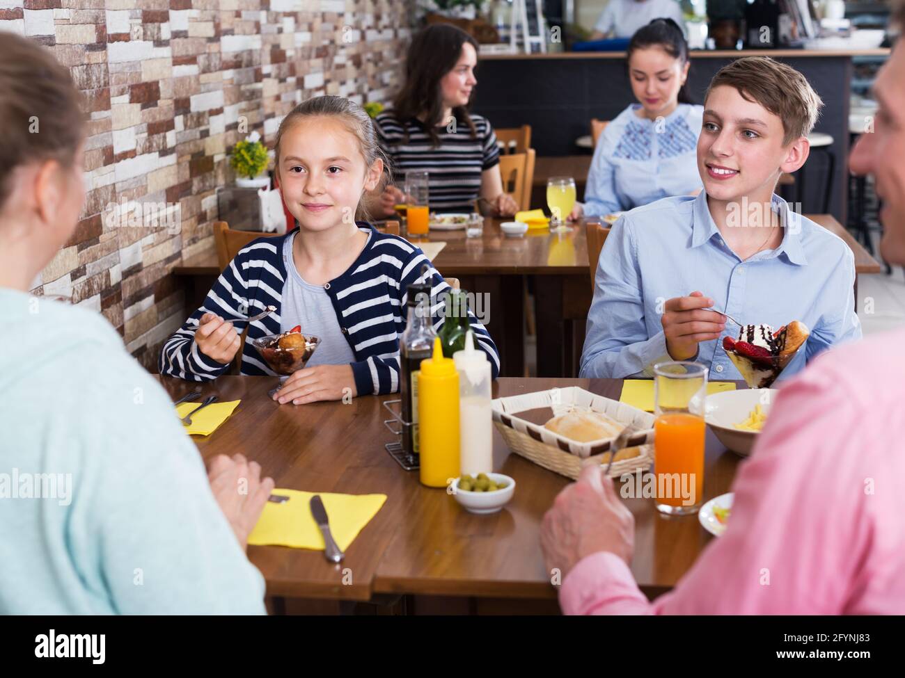 Smiling parents with kids having conversation at dining table in cafe ...