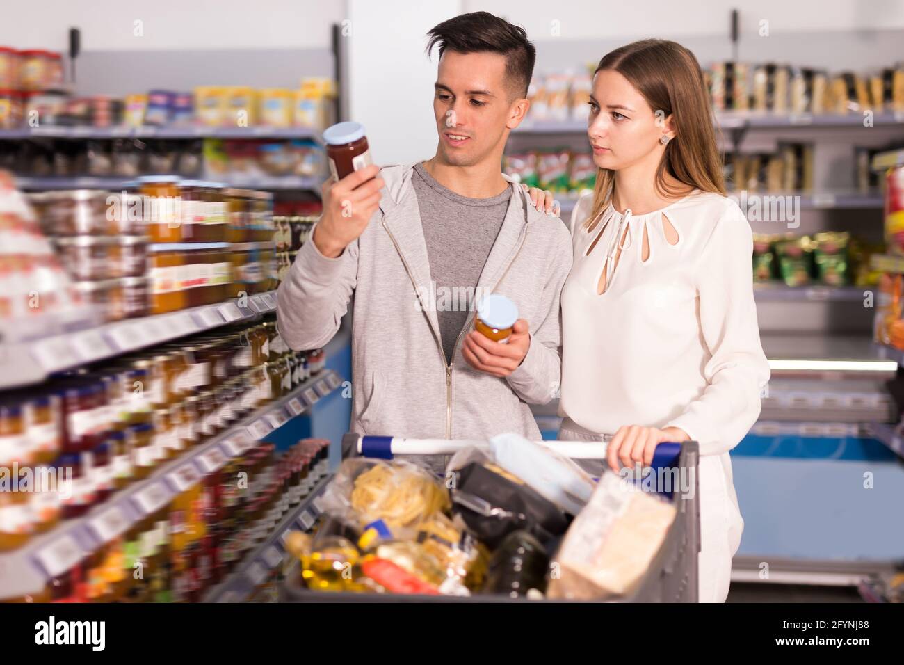 Positive couple shopping together, choosing preserved food products at ...