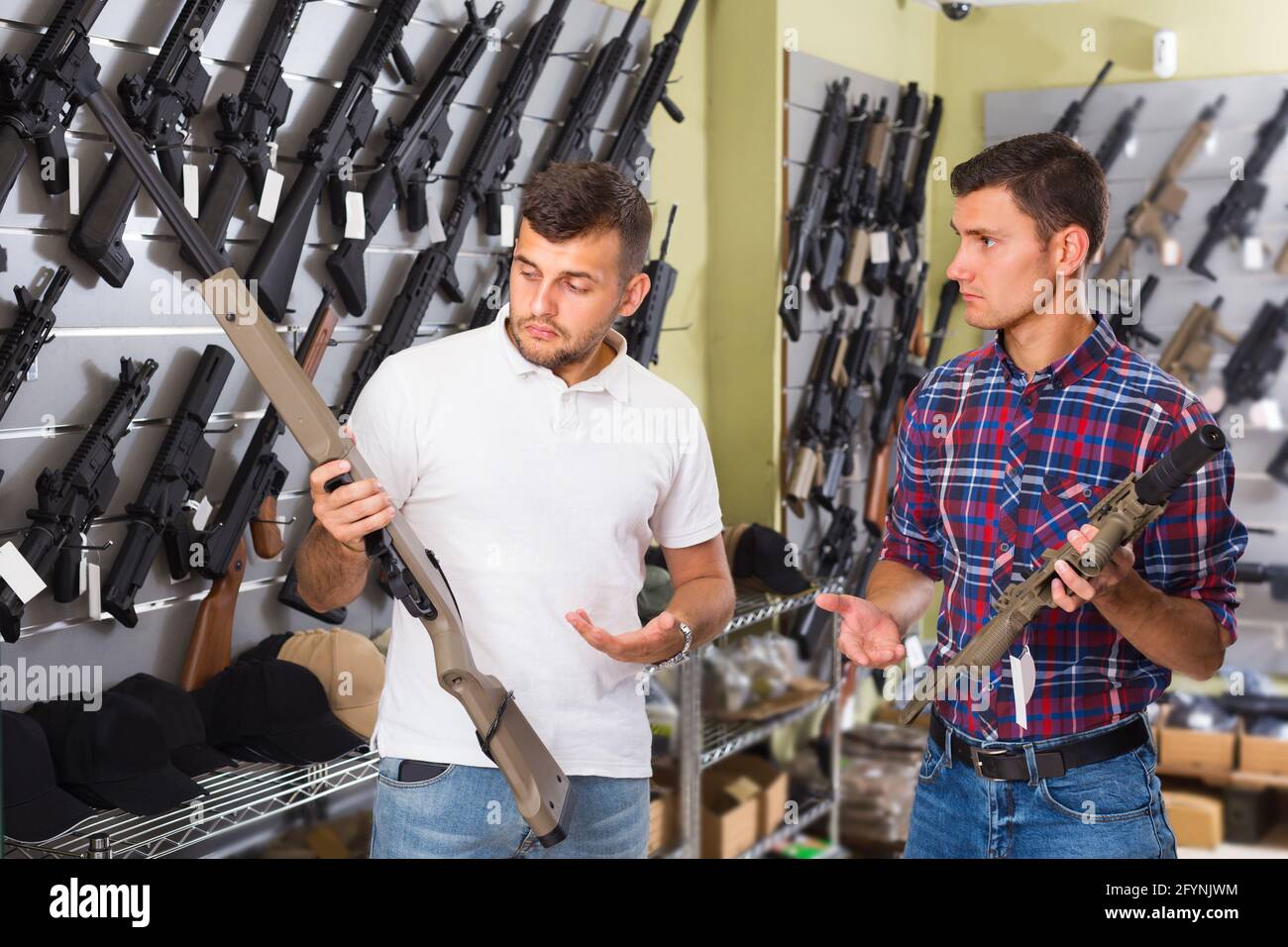 Two friends are choosing pneumatic rifle in airsoft store Stock Photo ...