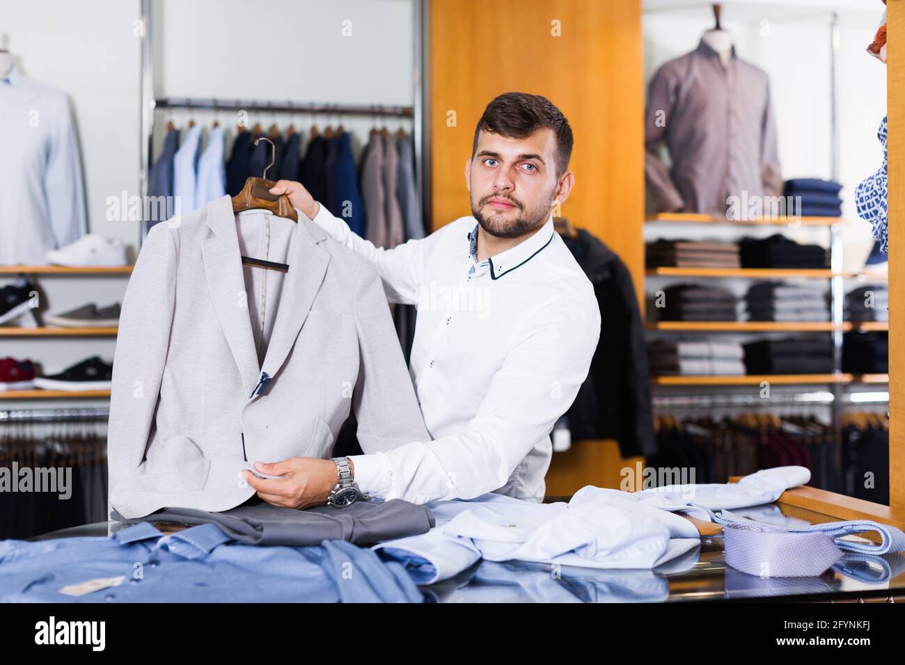 Happy male shopping assistant offering various jacket in men clothes ...