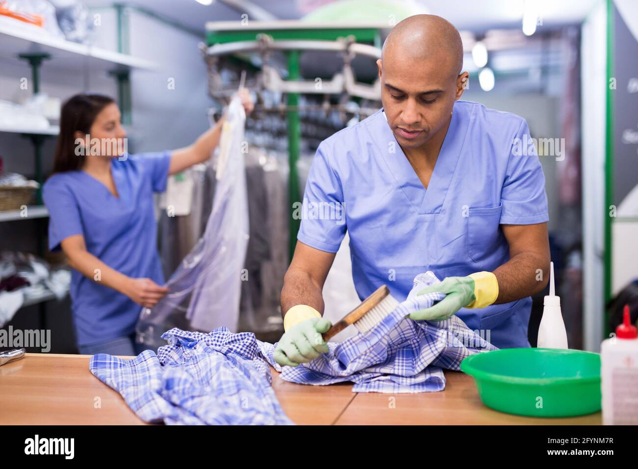 Confident man laundry worker cleaning shirt using brush at dry-cleaning ...