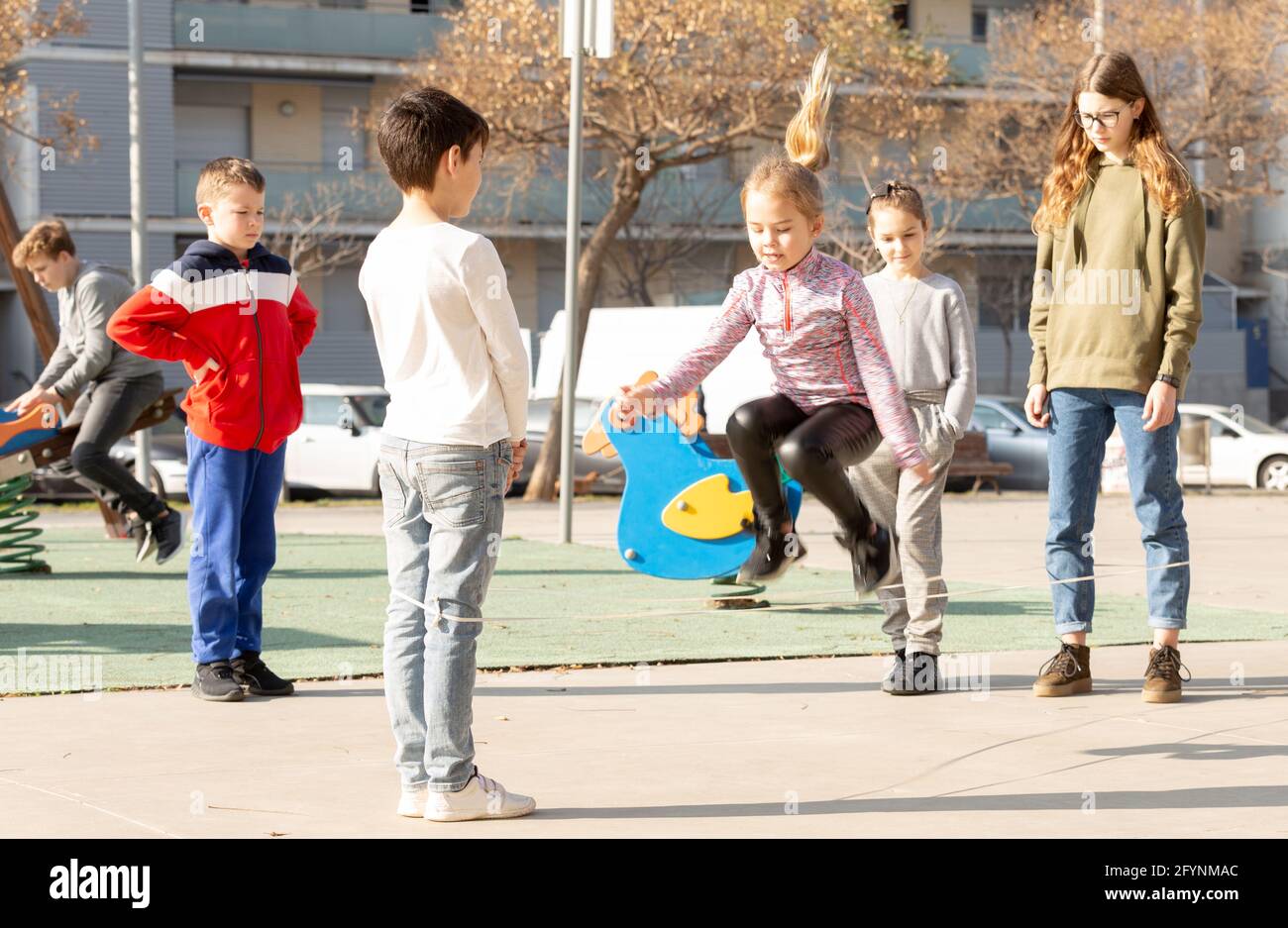 Group of children playing outdoors jumping on rubber band at sunny day ...