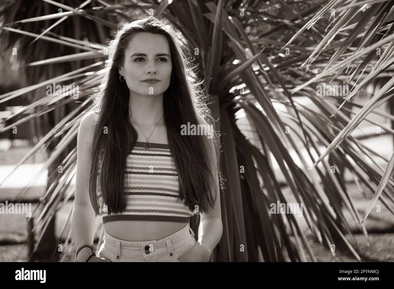 Portrait of a young brunette woman standing near a palm tree in a park ...