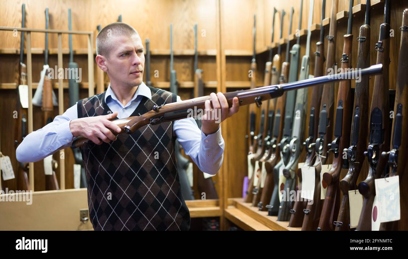 Confident male hunter examining hunting shotgun before buying in gun ...