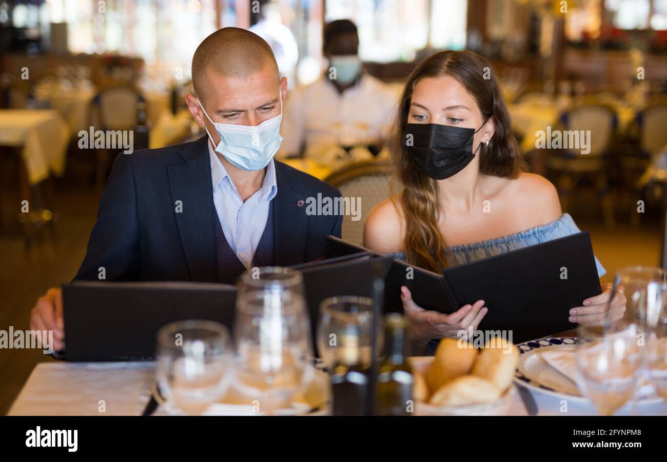 Couple in protective face masks choosing meals reading menu at ...