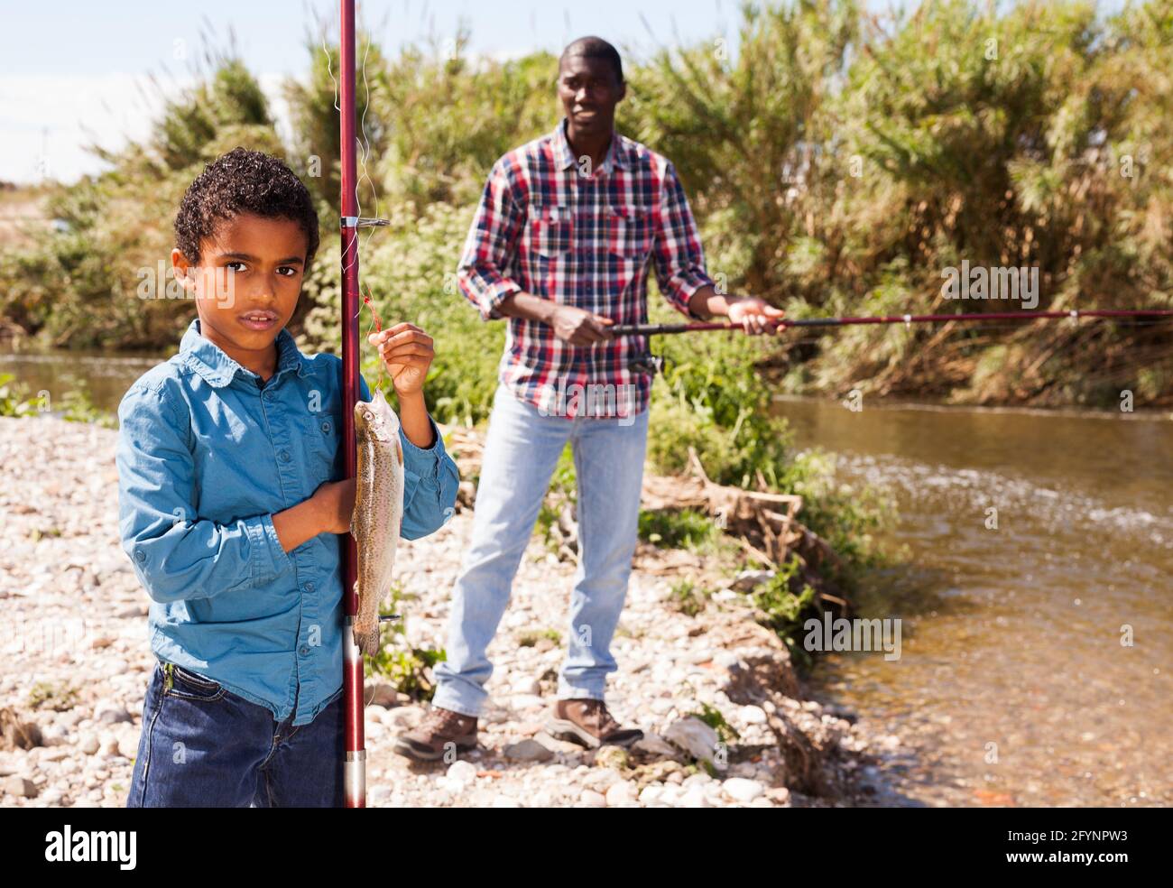 Portrait of afro fisherman and his little son holding fishing rod with ...